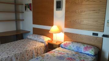 Quarto com duas camas de solteiro, mesa de cabeceira com luminária, cabeceiras de madeira, relógio de parede e decoração de borboleta.