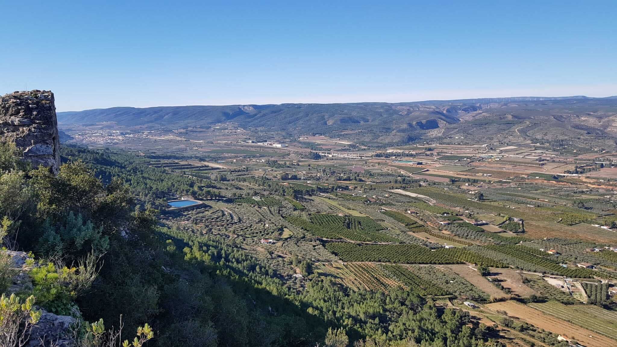 Vista panorâmica de um vale com campos em socalcos, uma pequena massa de água e um afloramento rochoso.
