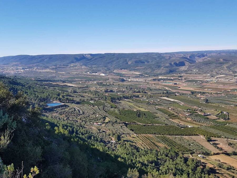 Vista panorâmica de um vale com campos em socalcos, uma pequena massa de água e um afloramento rochoso.