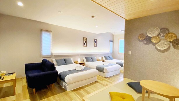 Quarto de hotel com duas camas, um sofá, uma mesinha e um painel decorativo.