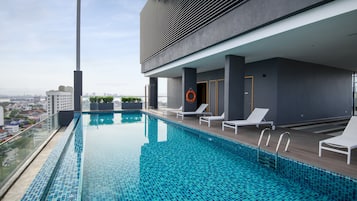 Piscina infinita no terraço com espreguiçadeiras, vista da cidade e estrutura de edifício moderno.
