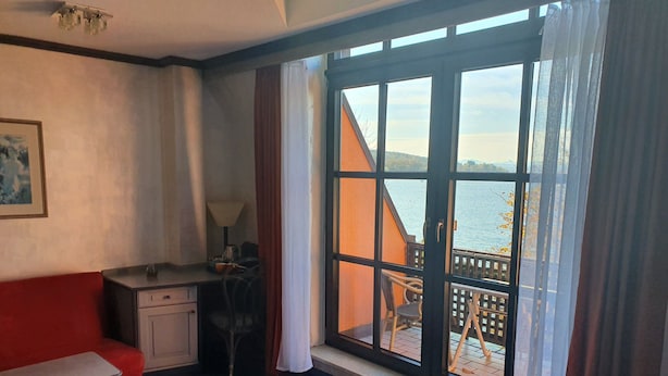 Quarto de hotel com cama, escrivaninha, cadeira e vista para a água.