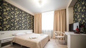 Quarto de hotel com cama, mesa de cabeceira, cadeira, escrivaninha e televisão.