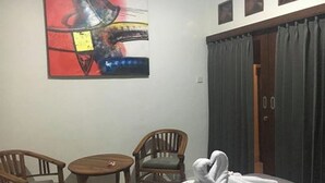 Quarto de hotel com cama, duas cadeiras de madeira, uma mesinha e um quadro na parede.