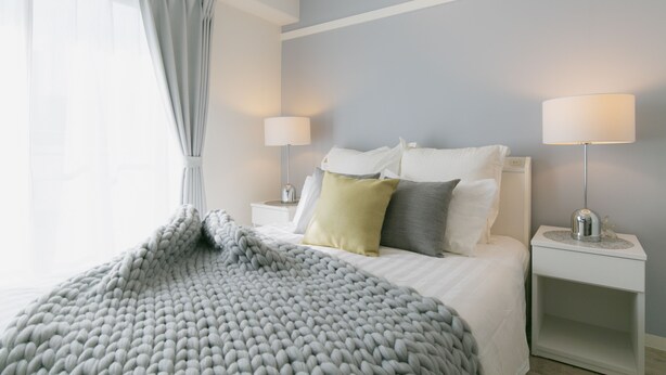 Quarto moderno com cama grande, duas mesas de cabeceira com luminárias e janela com cortinas leves.