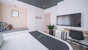 Quarto de hotel moderno com uma cama grande, uma escrivaninha, televisão de tela plana e um vaso de plantas.