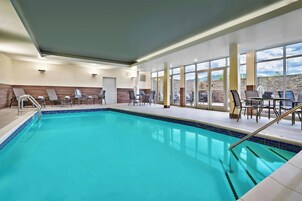 Uma piscina interior com água azul cristalina, rodeada por espreguiçadeiras e mesas.