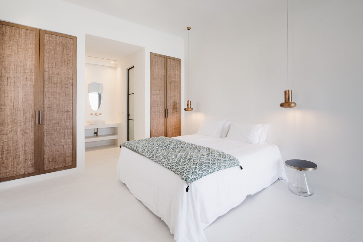 Quarto com cama grande, mesa de cabeceira, luminária pendente e guarda-roupa.