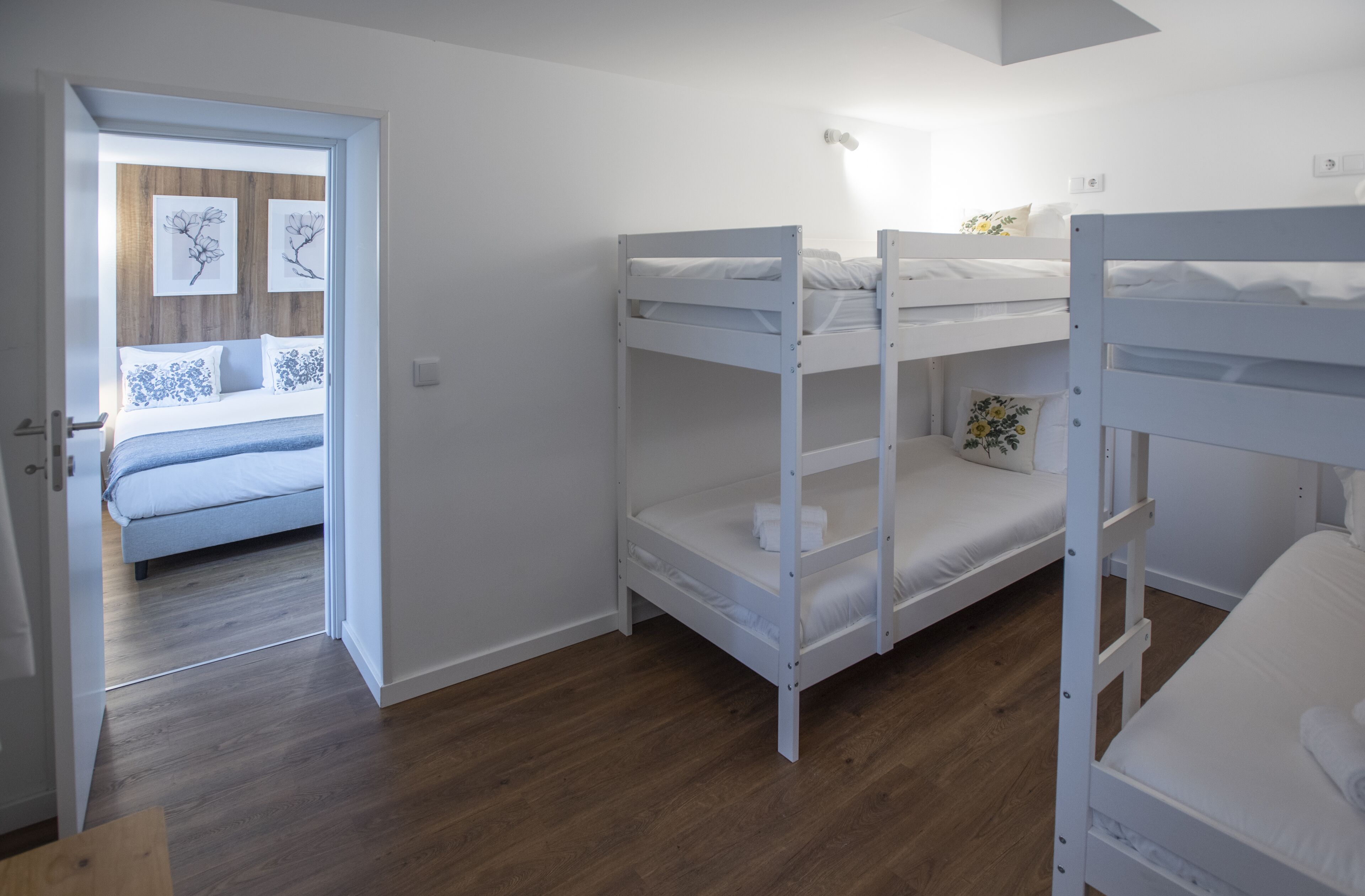 Quarto com beliches, porta que dá para outro espaço e piso de madeira.