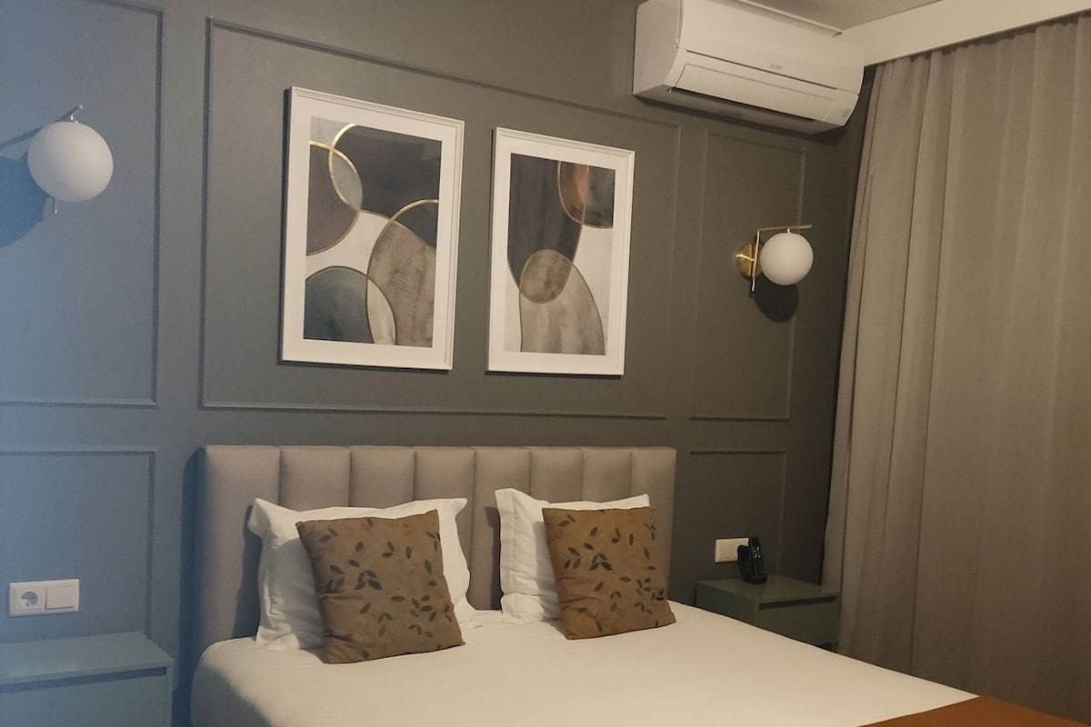 Quarto de hotel com uma cama, dois lustres fixados na parede e duas pinturas abstratas emolduradas.