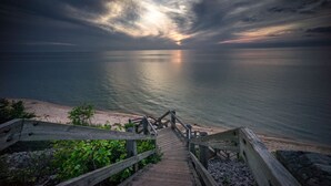 Uma escadaria de madeira que leva a uma praia com o sol se pondo ao fundo.