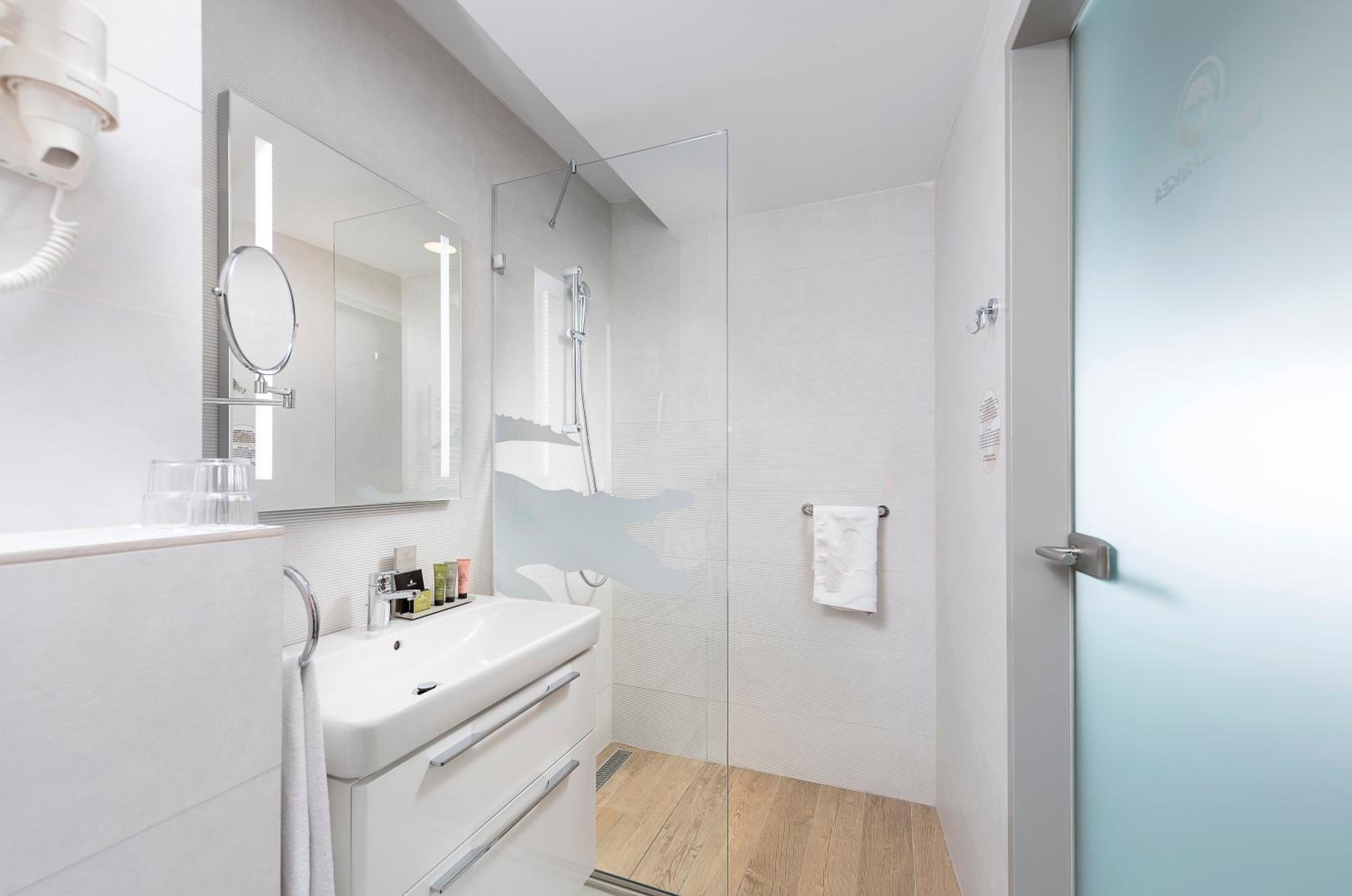 Uma casa de banho moderna com lavatório branco, espelho e chuveiro.