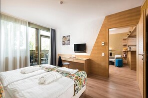 Quarto de hotel com cama, escrivaninha, televisão e banheiro visível por uma porta aberta.
