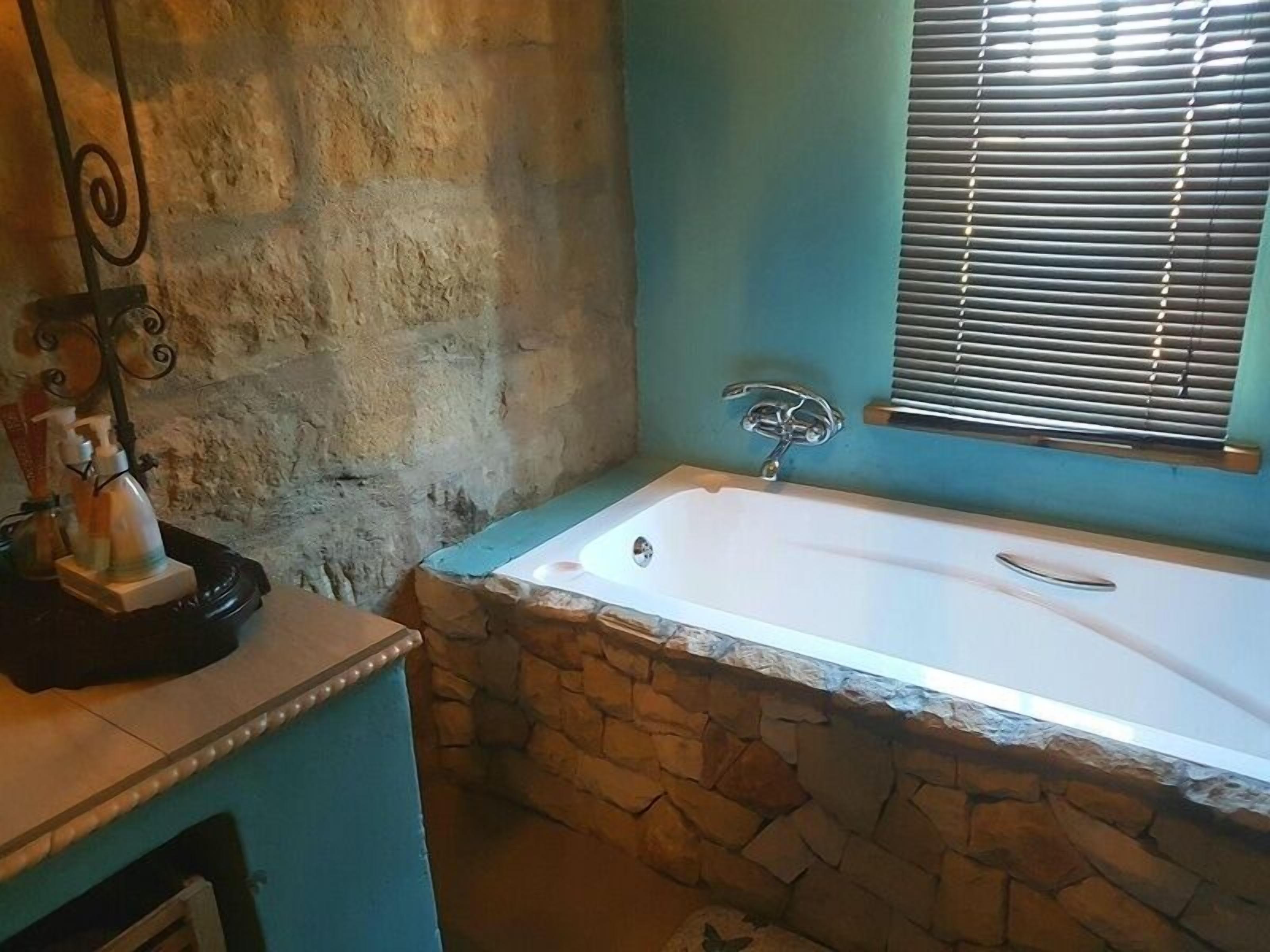 Um banheiro com parede de pedra, banheira, janela com persianas e um objeto decorativo no balcão.