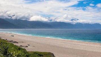 Uma praia com céu claro, montanhas ao fundo e mar calmo.