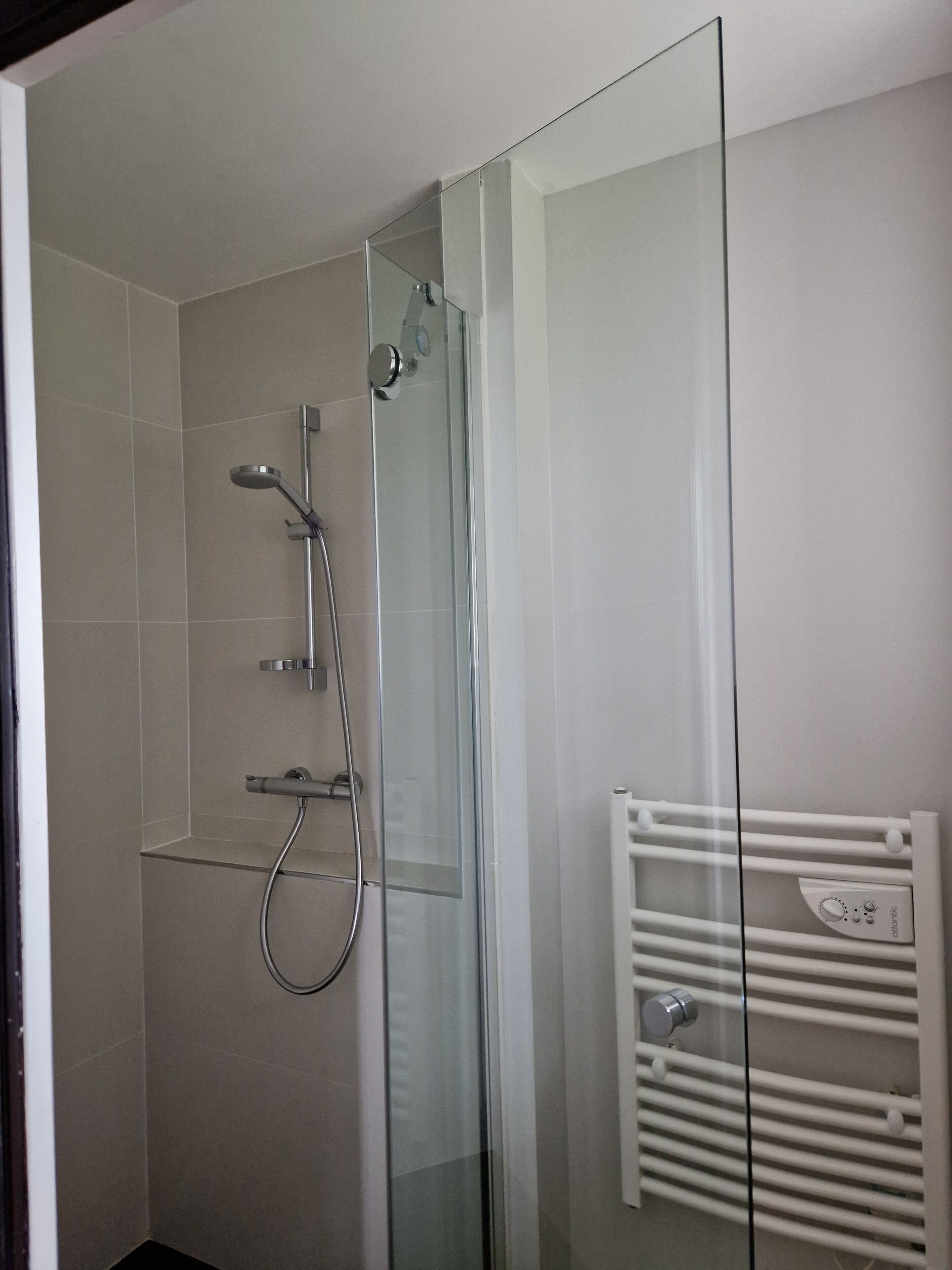 Um chuveiro moderno com divisória de vidro, chuveiro manual e painel de controle fixado na parede.