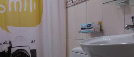 Casa de banho com sanita, lavatório e cortina de chuveiro com padrão de rosto sorridente.