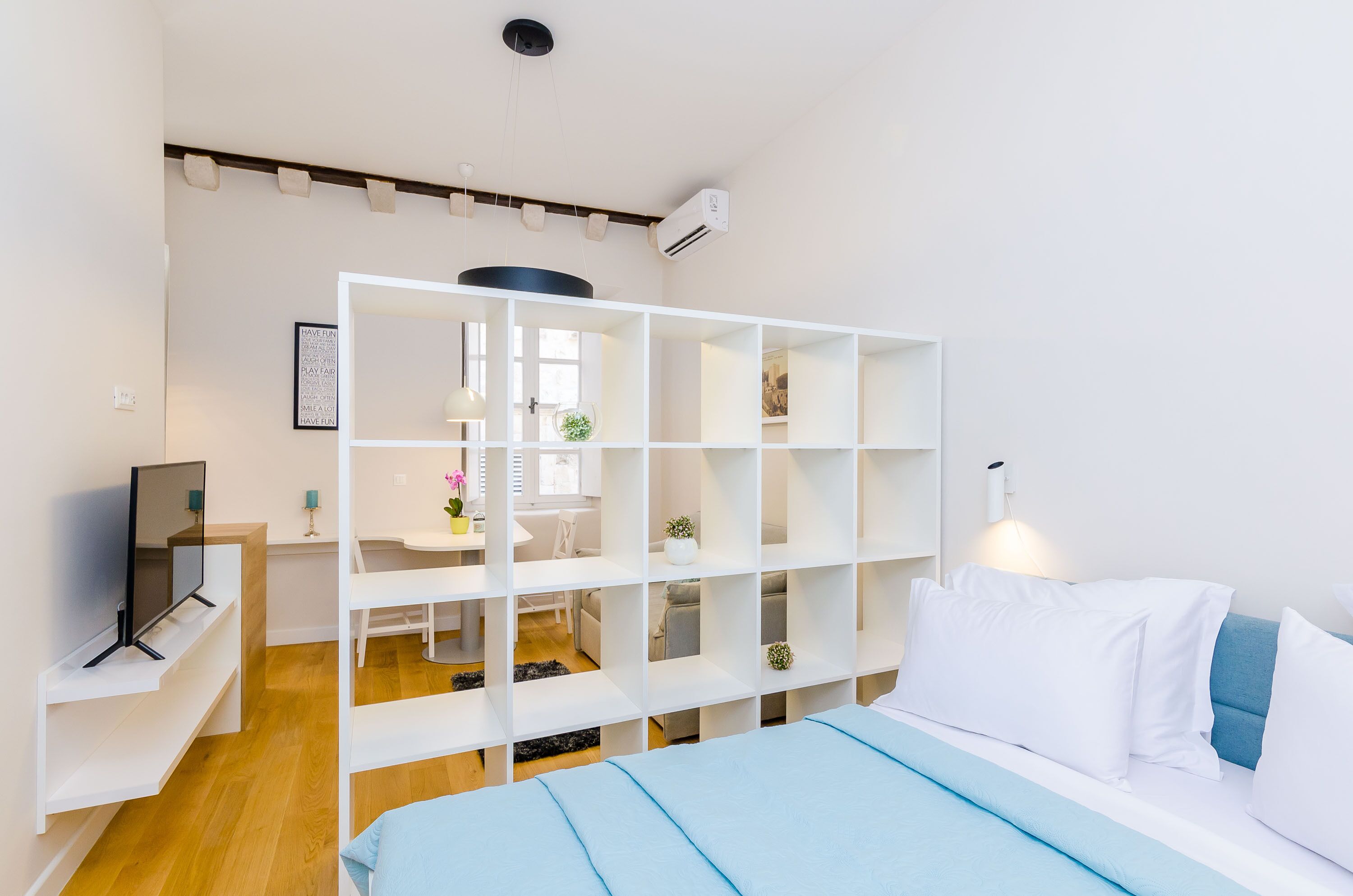 Quarto moderno com cama, estante branca e TV em móvel.