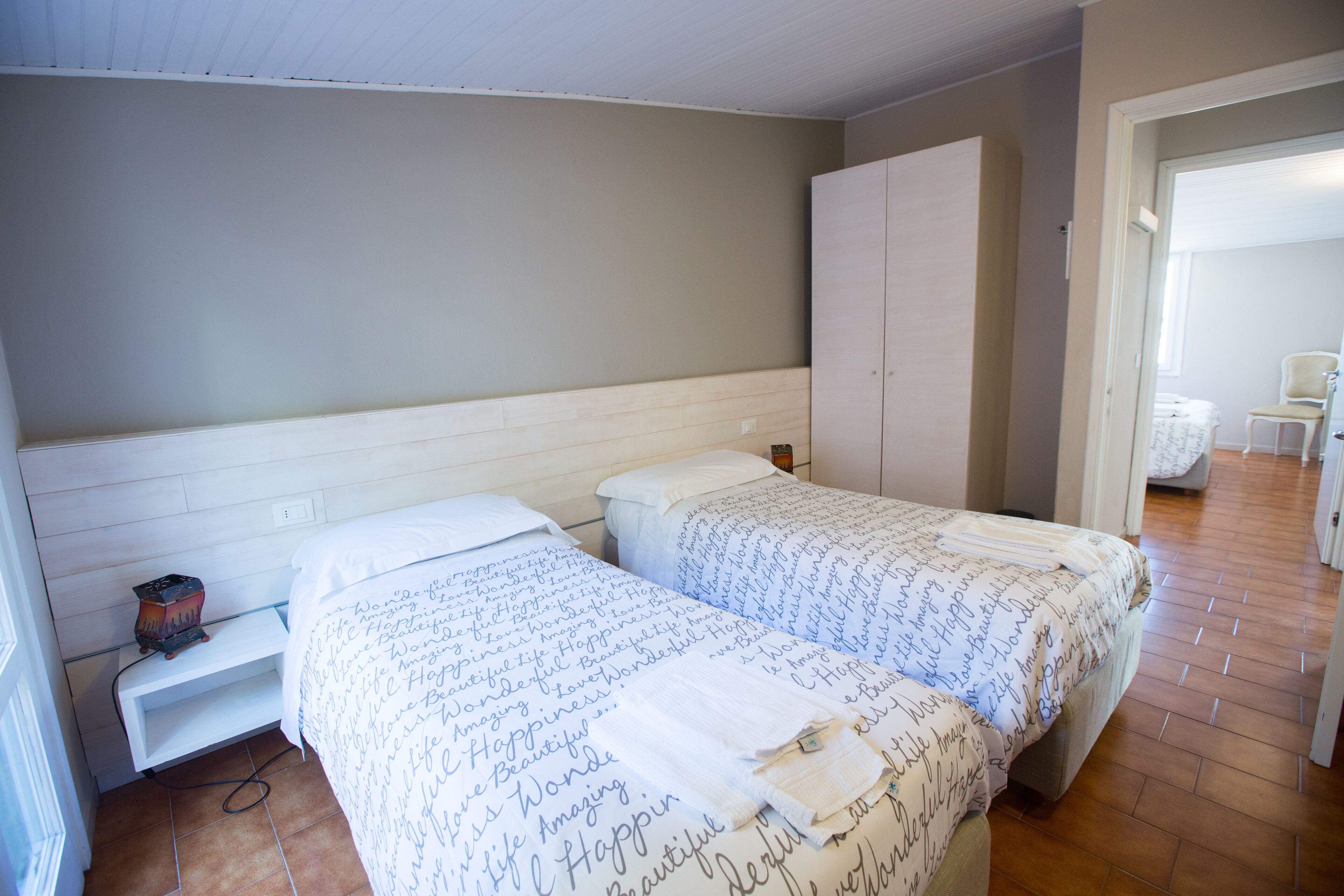 Quarto com duas camas, uma mesa de cabeceira e um guarda-roupa.