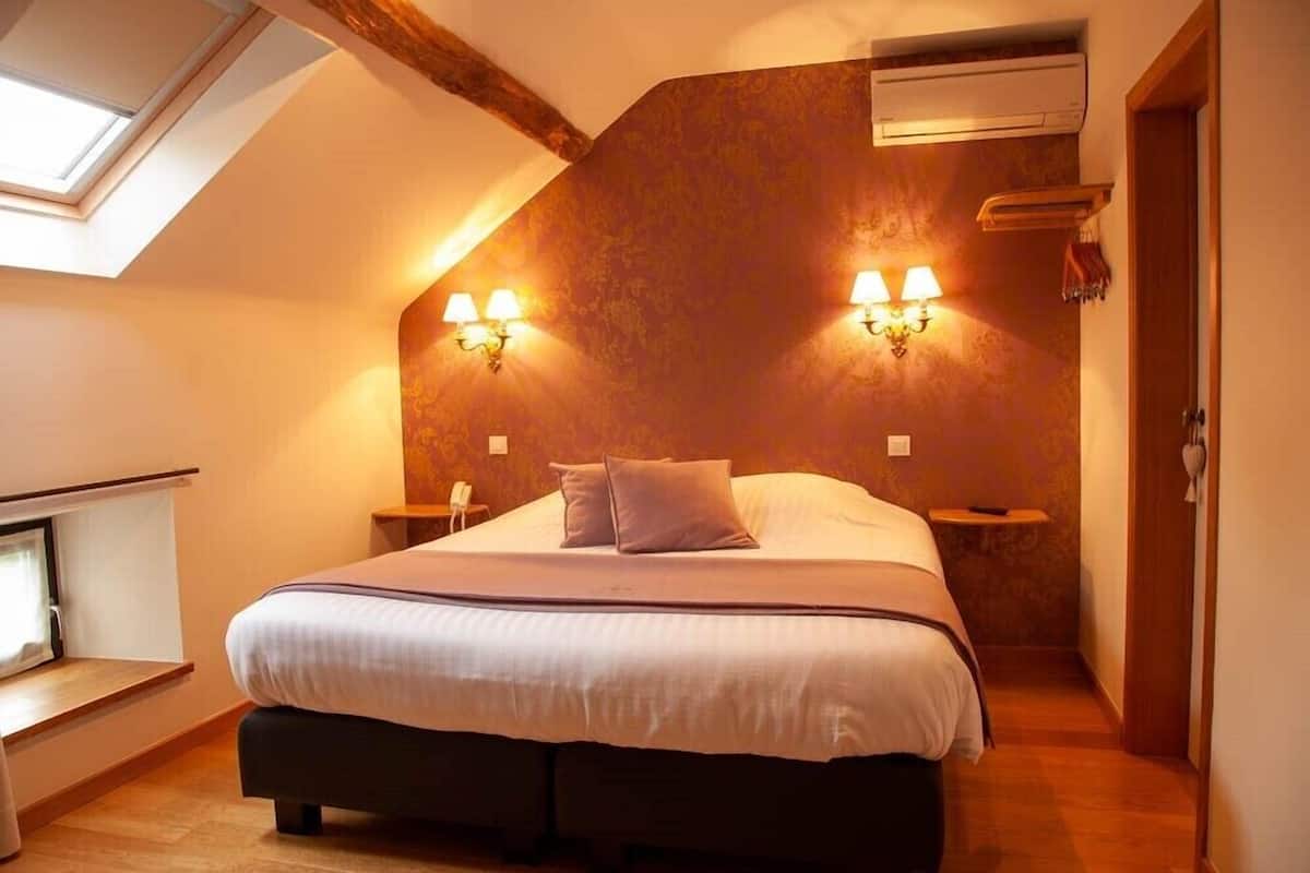 Quarto com uma cama grande, duas luminárias de cabeceira, um claraboia e teto de madeira.