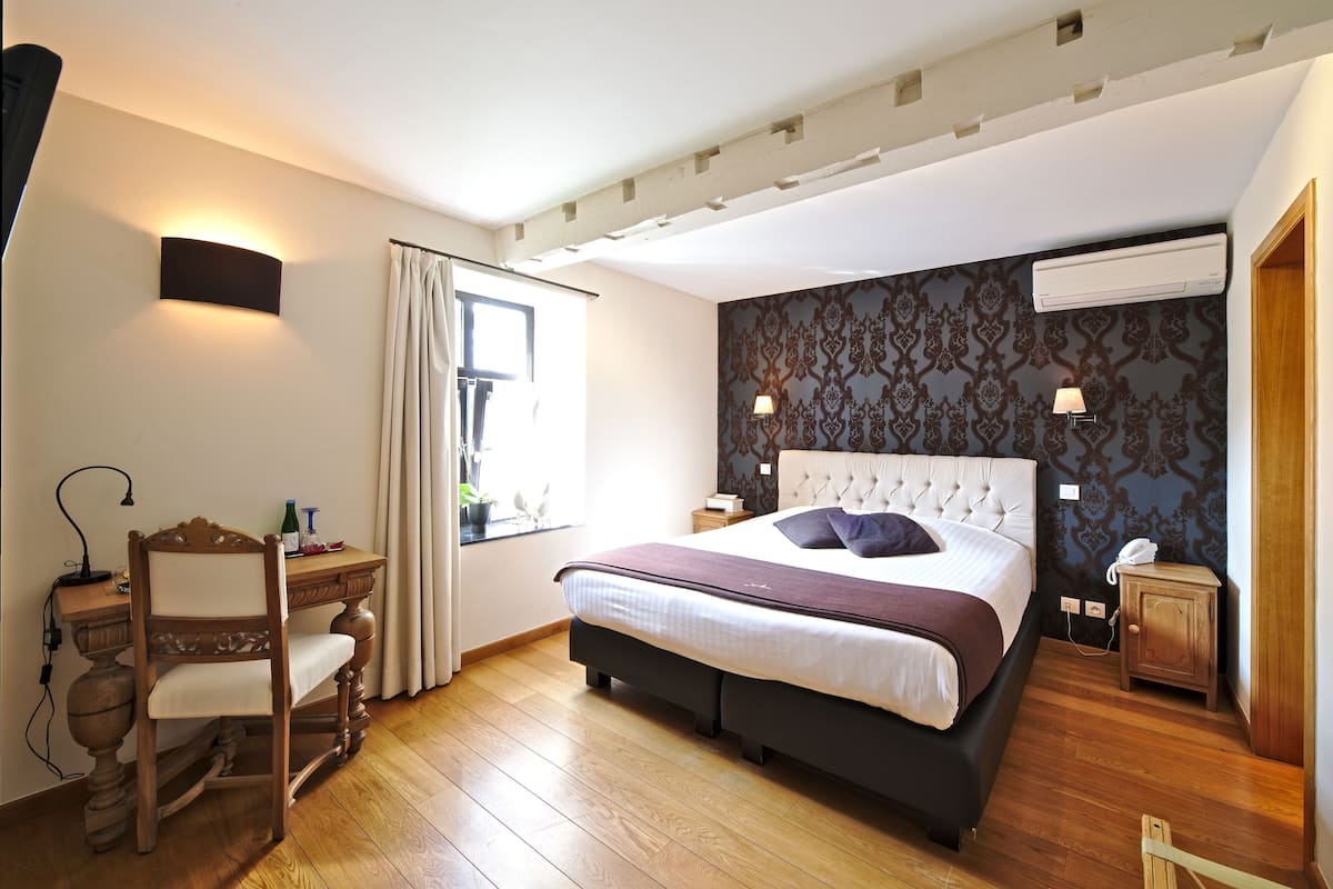 Quarto com cama, escrivaninha, cadeira e janela com cortinas.