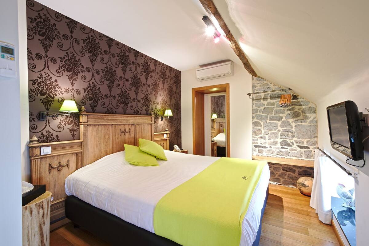 Quarto com uma cama grande, cabeceira de madeira, duas luminárias de cabeceira, parede de pedra e uma televisão.