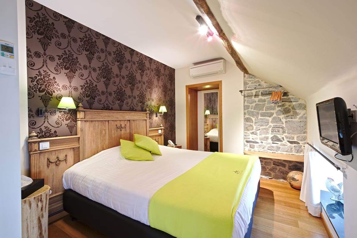 Quarto com cama, cabeceira de madeira, luminárias, parede de pedra e uma televisão.
