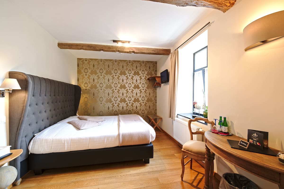 Quarto com uma cama grande, uma escrivaninha com cadeira, televisão e janela com cortinas.
