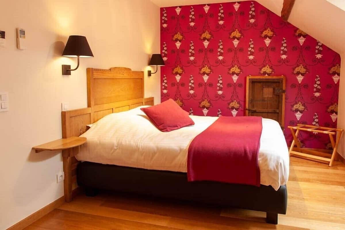 Quarto com cama de madeira, parede com padrão vermelho e duas luminárias fixadas na parede.