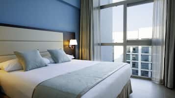 Quarto de hotel com uma cama grande, uma mesa de cabeceira com abajur e vista para edifícios pela janela.