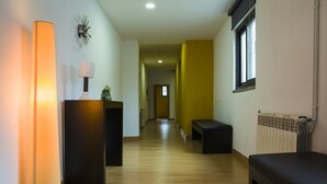 Um corredor com piso de madeira, radiador, um banco e uma luminária.