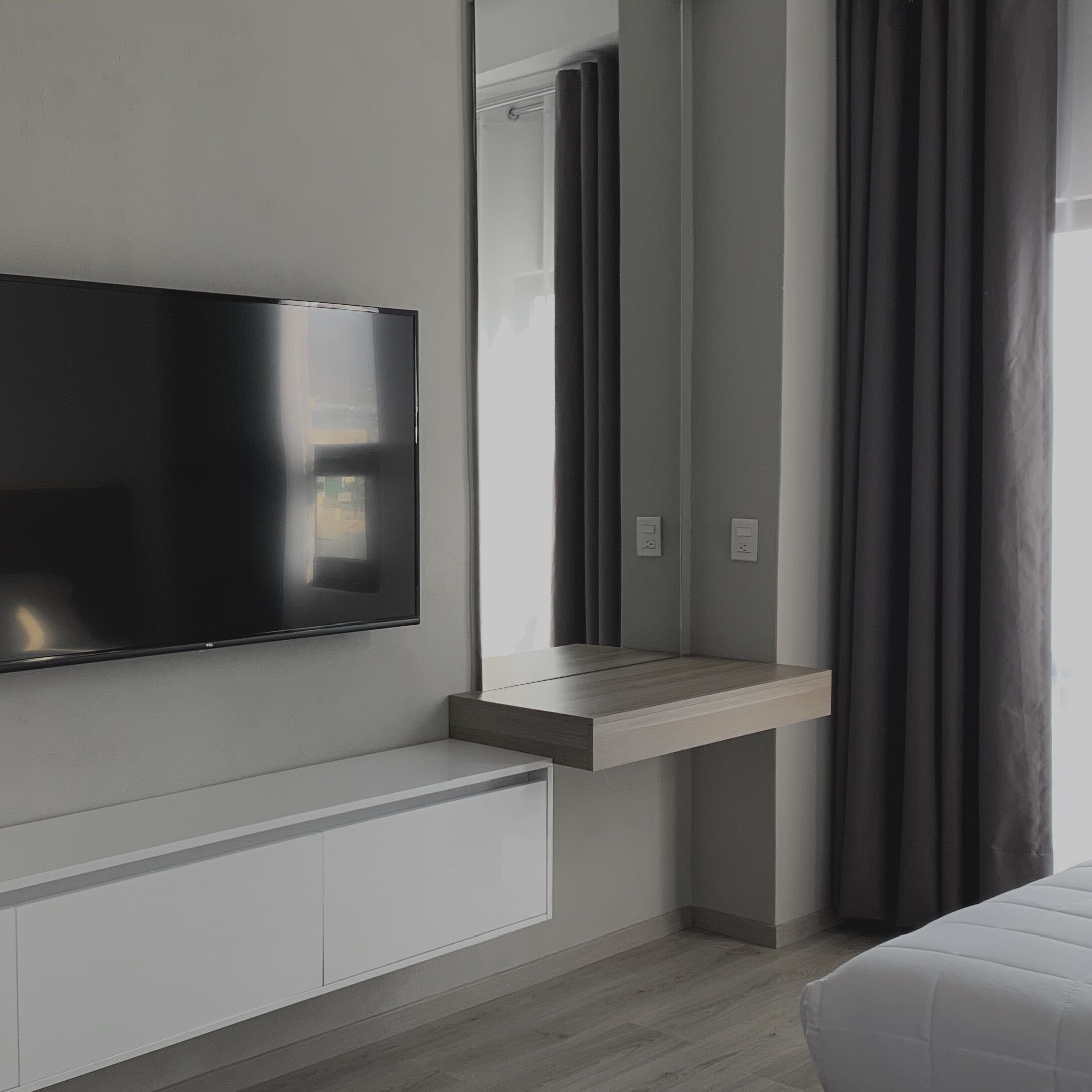 Quarto de hotel moderno com televisão de tela plana presa à parede, mesa consola de madeira e um espelho grande.