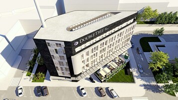 Um hotel moderno com design angular único, identificado como “DOUBLE TREE by Hilton”. Possui um terraço no terraço e um estacionamento com vários carros.