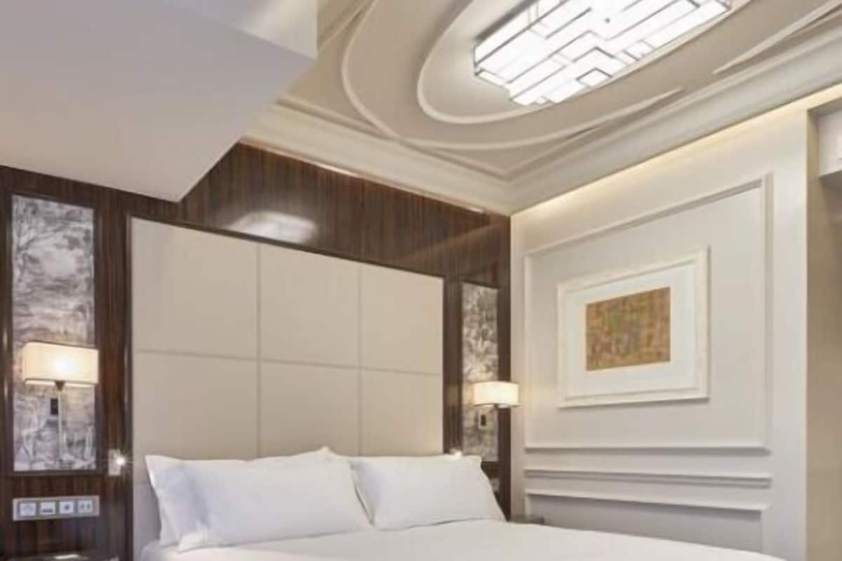 Quarto de hotel moderno com uma cama grande, uma mesa de cabeceira, uma luminária na parede e um lustre no teto.