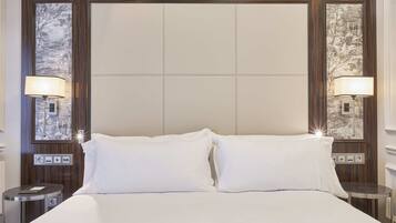Quarto de hotel com uma cama grande, duas mesas de cabeceira e cabeceira com painel decorativo.