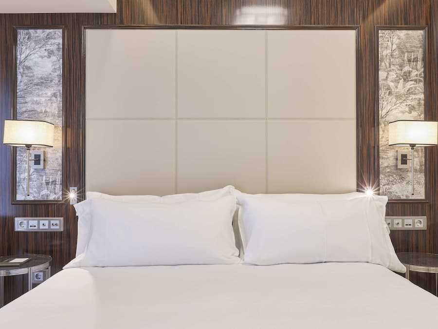 Quarto de hotel com uma cama grande, duas mesas de cabeceira e cabeceira com painel decorativo.