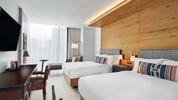 Quarto de hotel com duas camas, uma escrivaninha, uma cadeira, uma televisão e uma janela com cortinas.