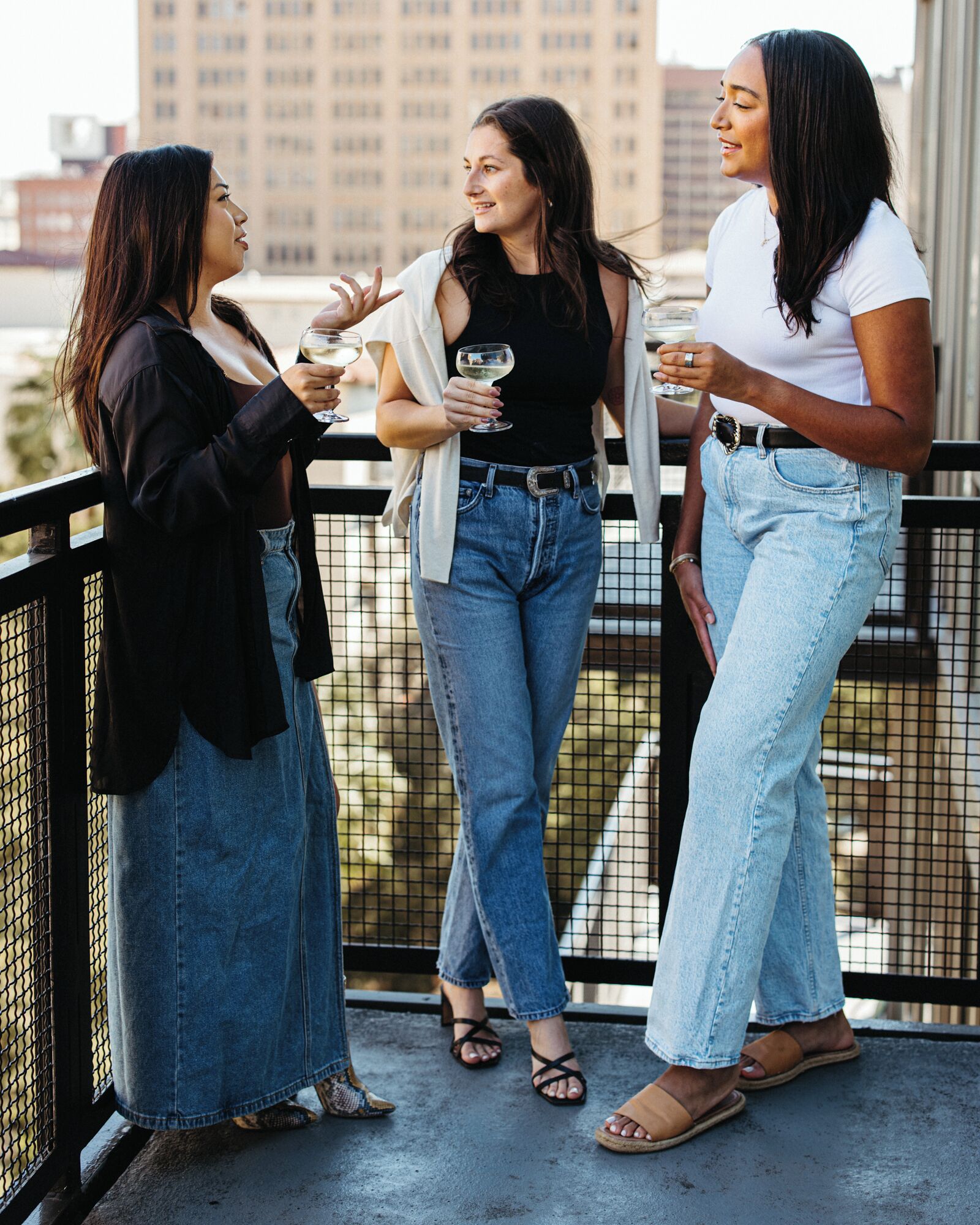 Três mulheres em uma varanda, segurando bebidas.