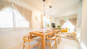 Uma sala de jantar moderna com uma mesa e cadeiras de madeira, um relógio na parede e uma televisão ao fundo.