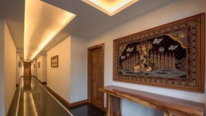 Um corredor com um banco de madeira, uma grande tapeçaria decorativa na parede e uma porta no final.