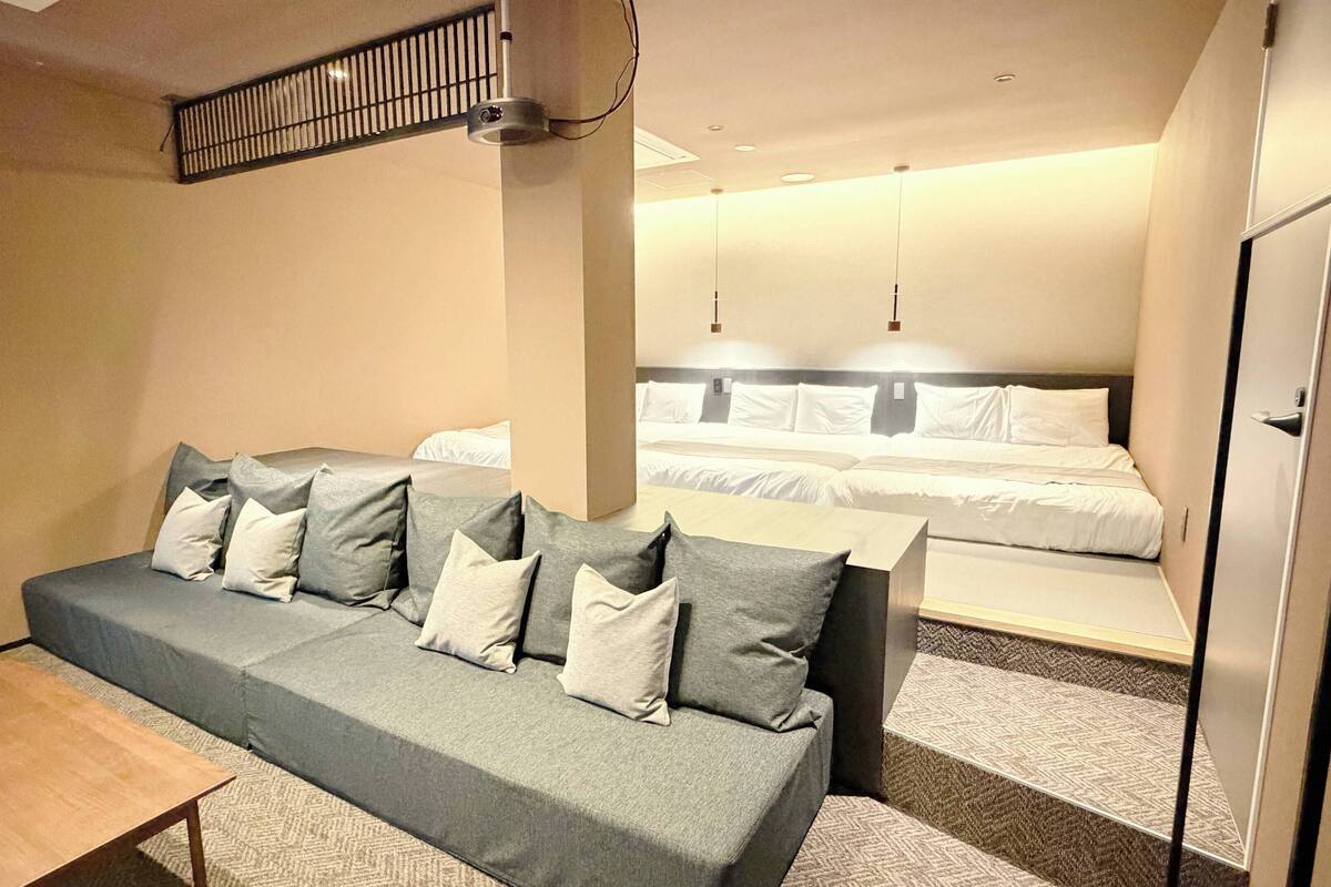 Quarto de hotel com sofá cinzento, uma mesa de madeira e uma cama com roupa de cama branca.