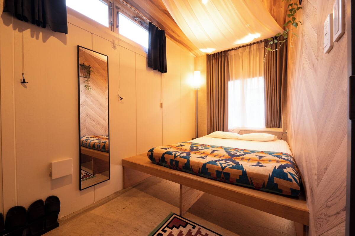 Quarto com cama, espelho, mesa de cabeceira, luminária e janela com cortinas.