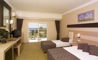 Quarto de hotel com duas camas, uma escrivaninha com televisão, uma varanda com vista e um quadro na parede.