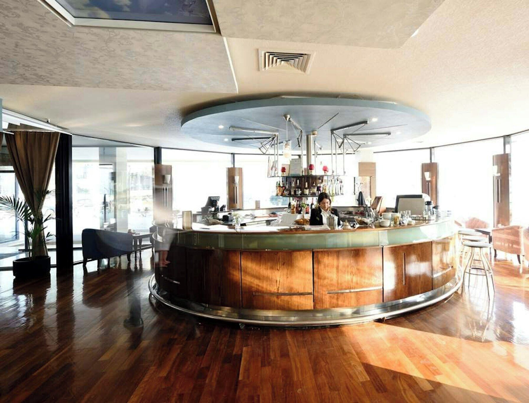 Uma área de bar moderna com balcão curvo, armários de madeira e teto com design geométrico singular.