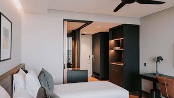 Quarto de hotel com duas camas, uma escrivaninha, uma cadeira, um ventilador de teto e um guarda-roupa.