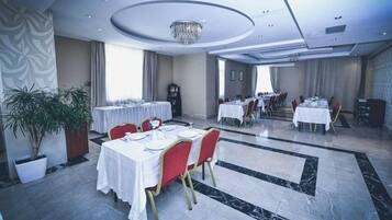 Uma sala de jantar espaçosa com várias mesas e cadeiras, um candelabro e um vaso de planta.