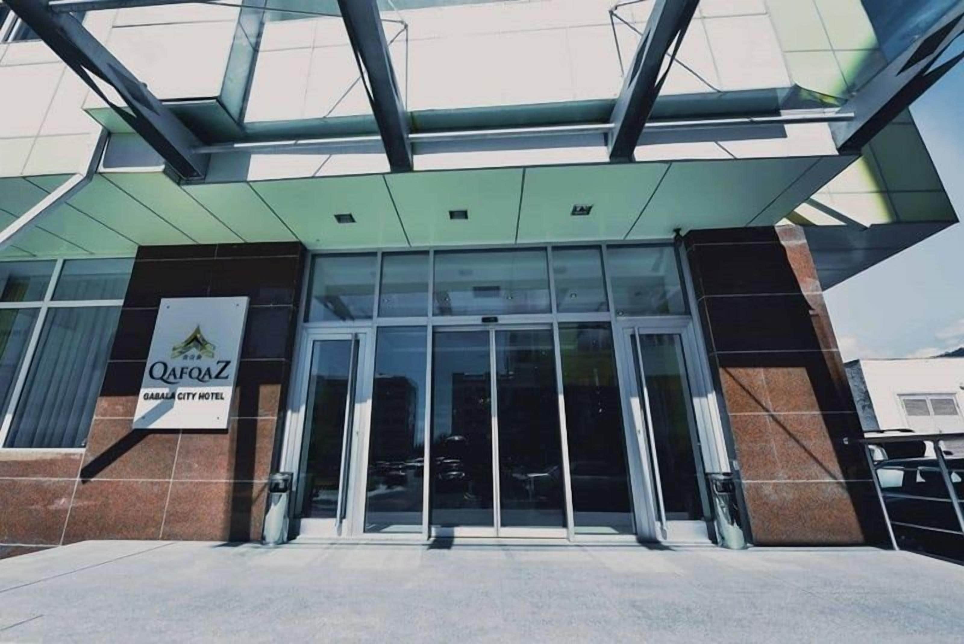 Entrada de hotel com fachada de vidro, placa de identificação e céu claro.