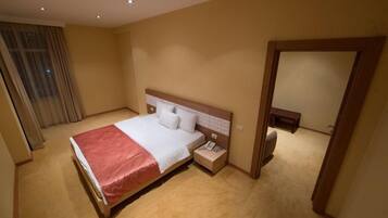 Quarto de hotel com cama, mesa de cabeceira e porta que dá para outro aposento.