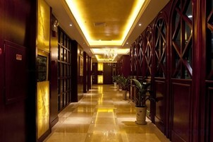Corredor de hotel com piso xadrez, painéis de madeira e plantas em vasos.