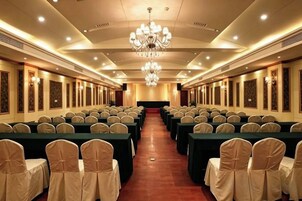 Uma sala de conferências com fileiras de mesas e cadeiras, um lustre e luminárias fixadas na parede.